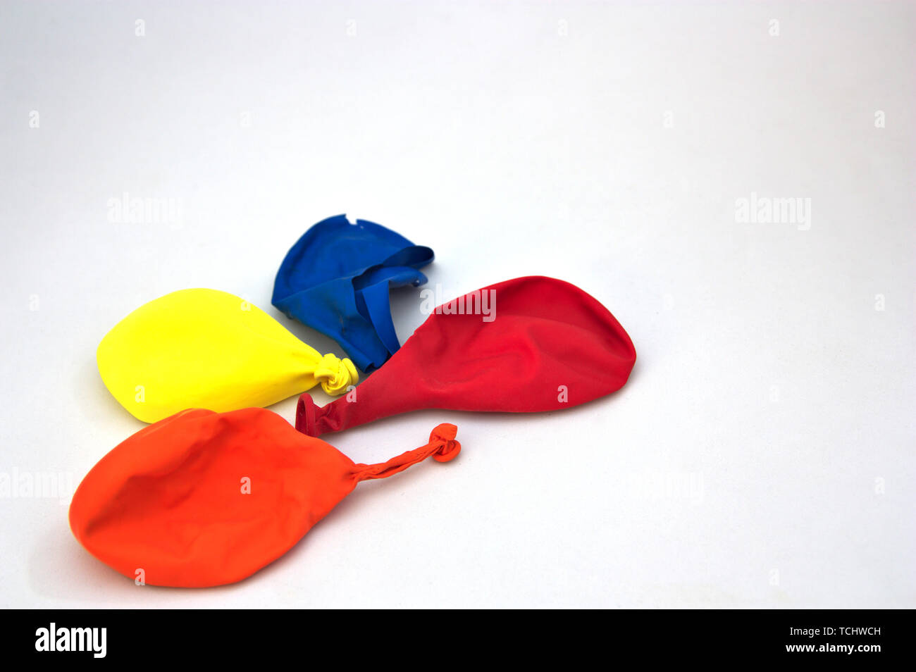 Four used, deflated and broken balloons of red, blue, orange and yellow ...