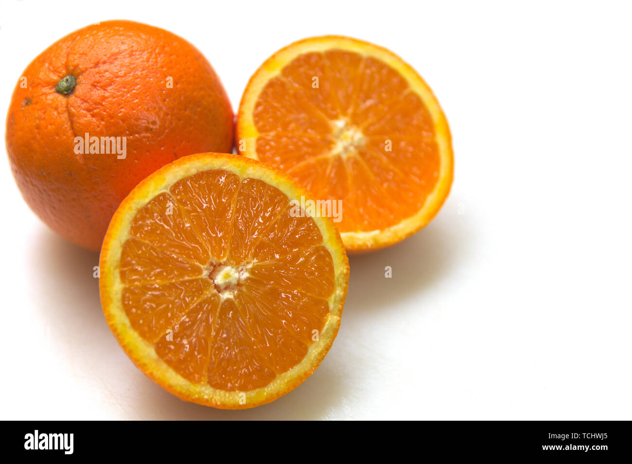 An orange split open in half next to another whole on a white table ...