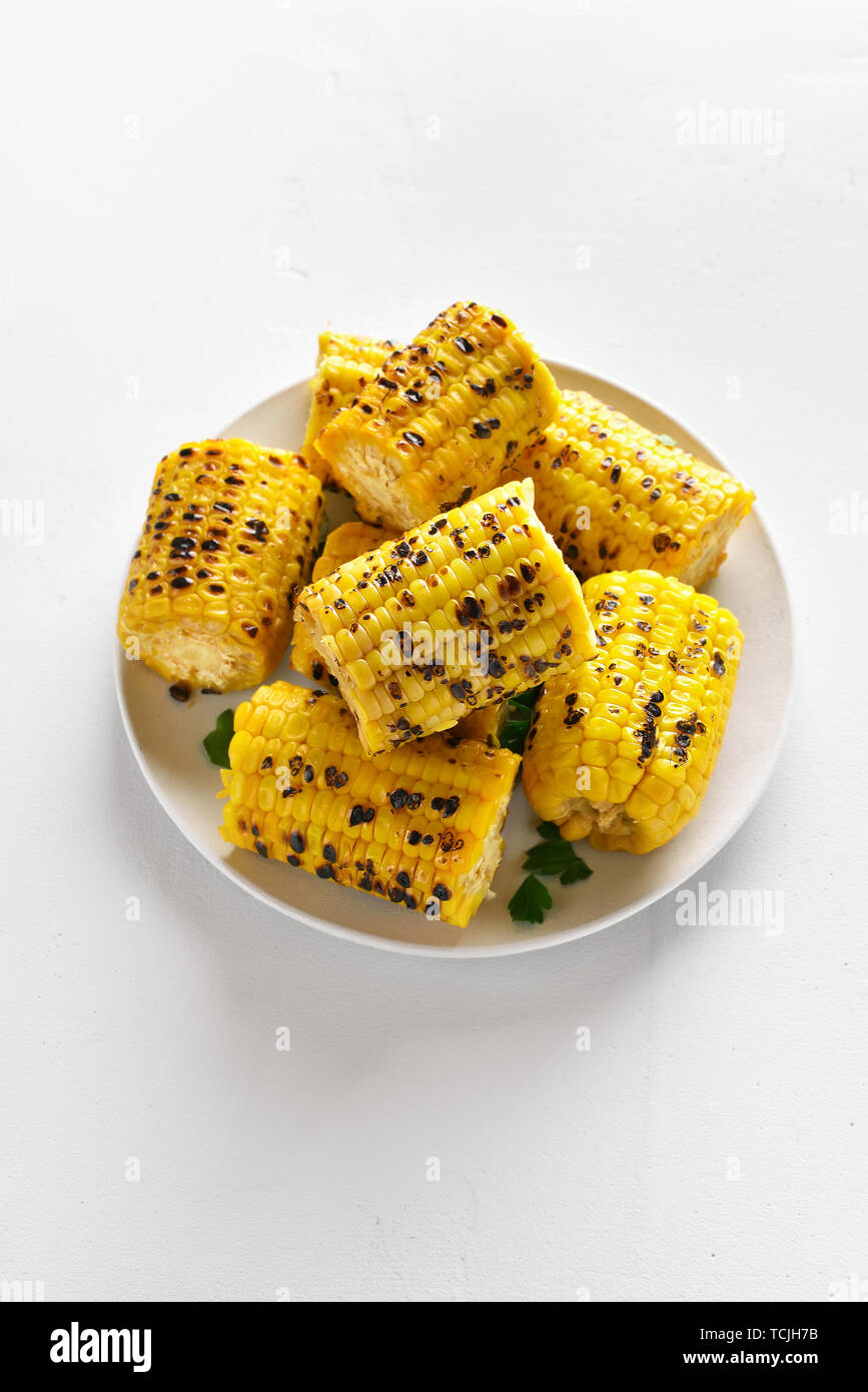Grilled corn cobs on plate over white stone background with copy space ...