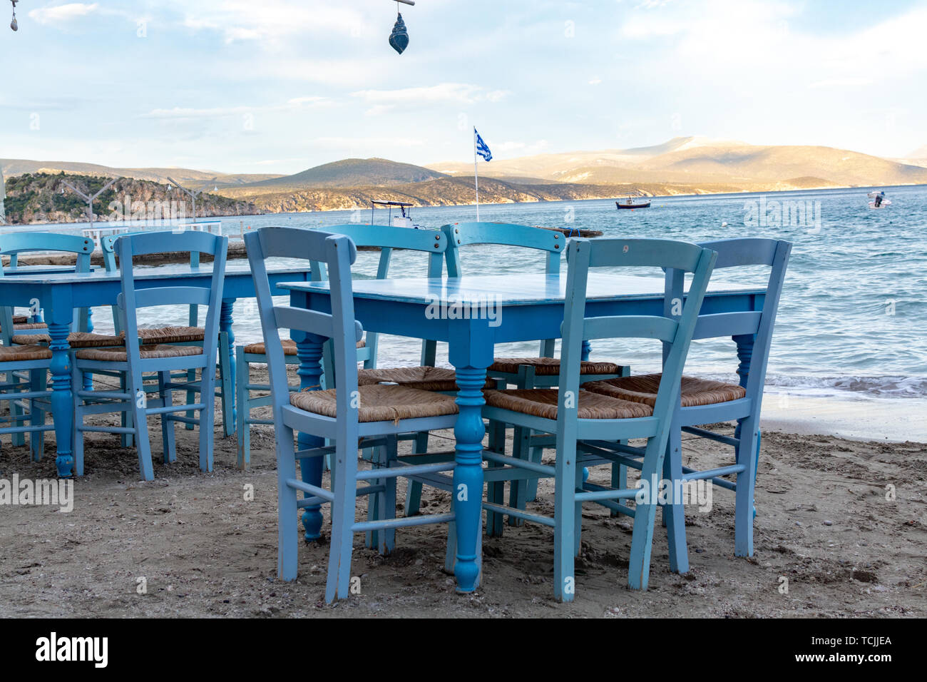 Traditional greek tavern with wooden tables on sandy beach near water ...