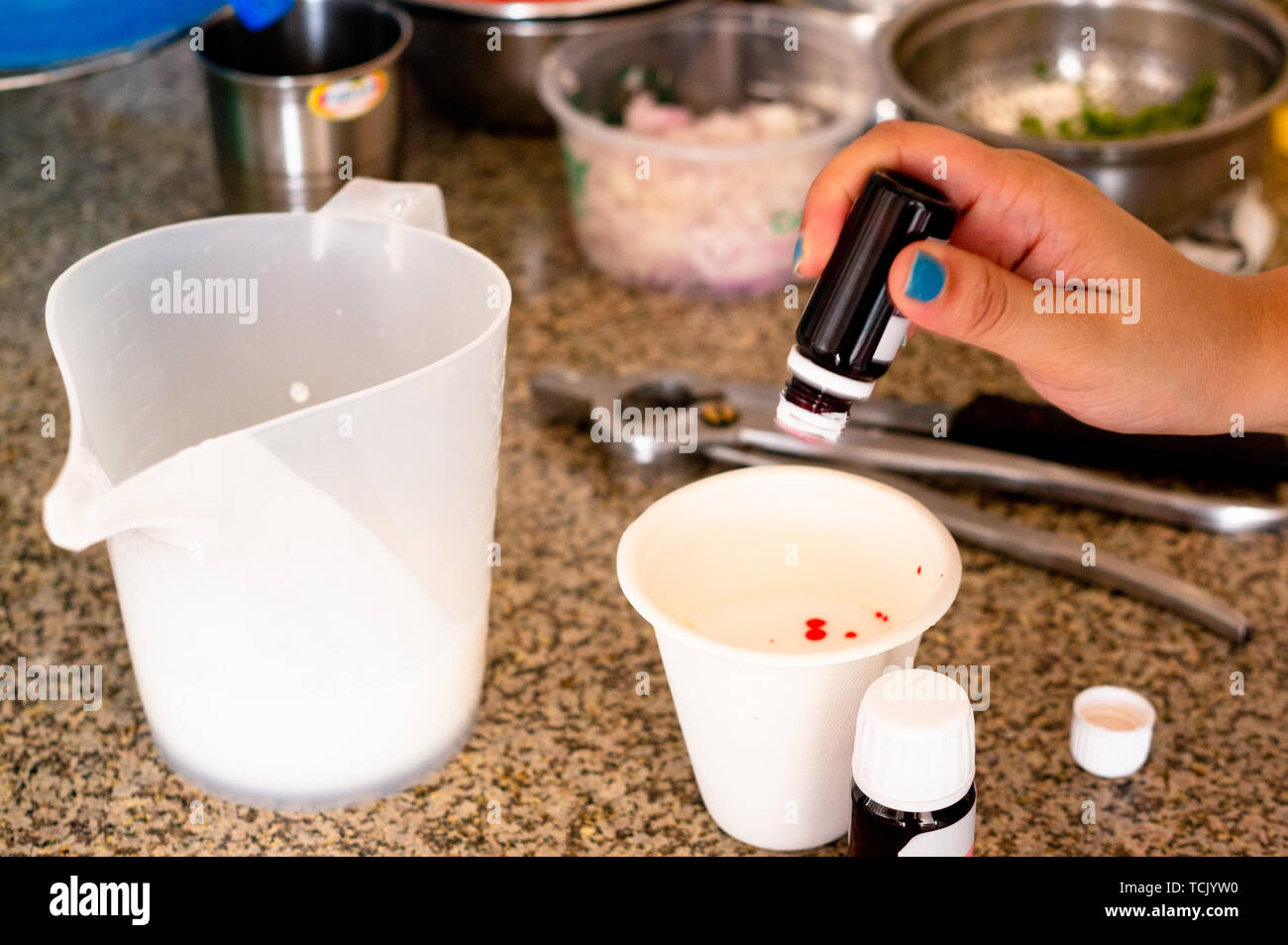 Female adding color drops to melted soap solution on kitchen counter ...