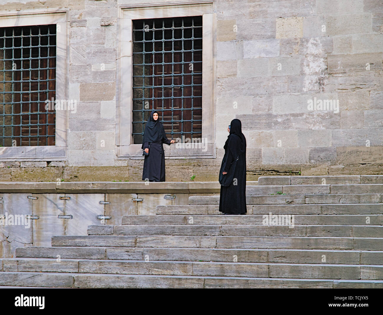 Two muslim women dressed with traditional black clothing, one taking ...