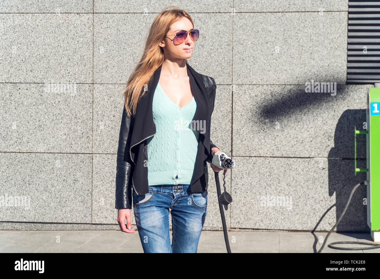 beautiful woman with electric plug in her hand goes to the car for ...