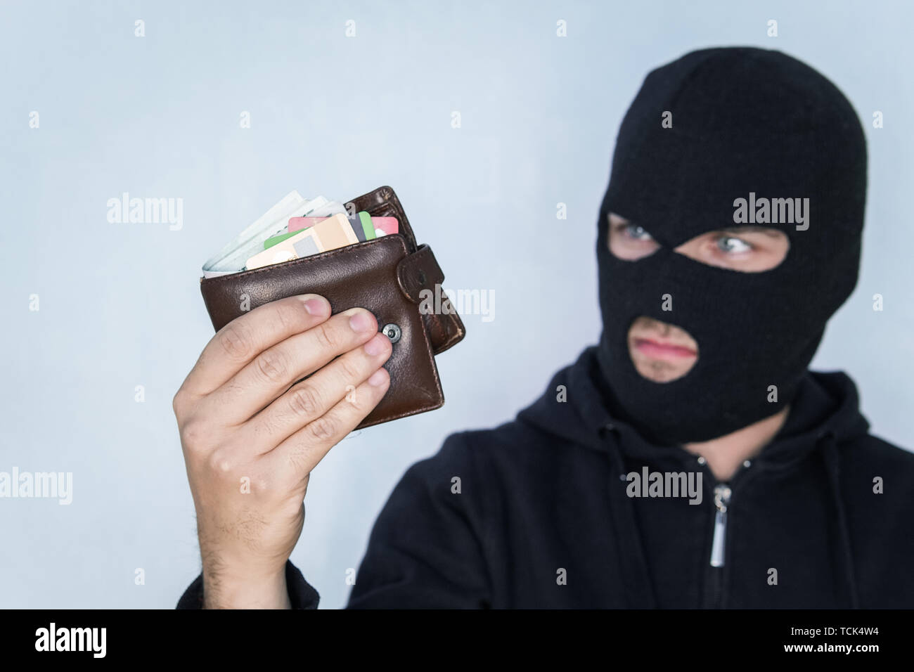 Thief in black mask holding wallet and looking at camera. The robber in ...