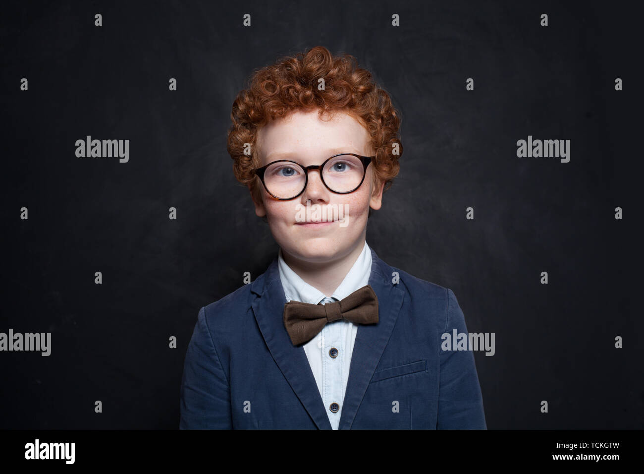 Cute child boy in suit and bow tie in classroom on chalkboard ...