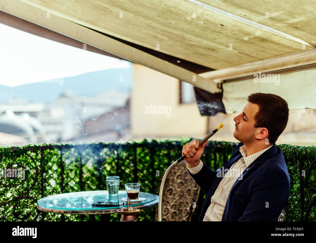 Elegant man chilling on balcony while smoke from hookah Stock Photo - Alamy