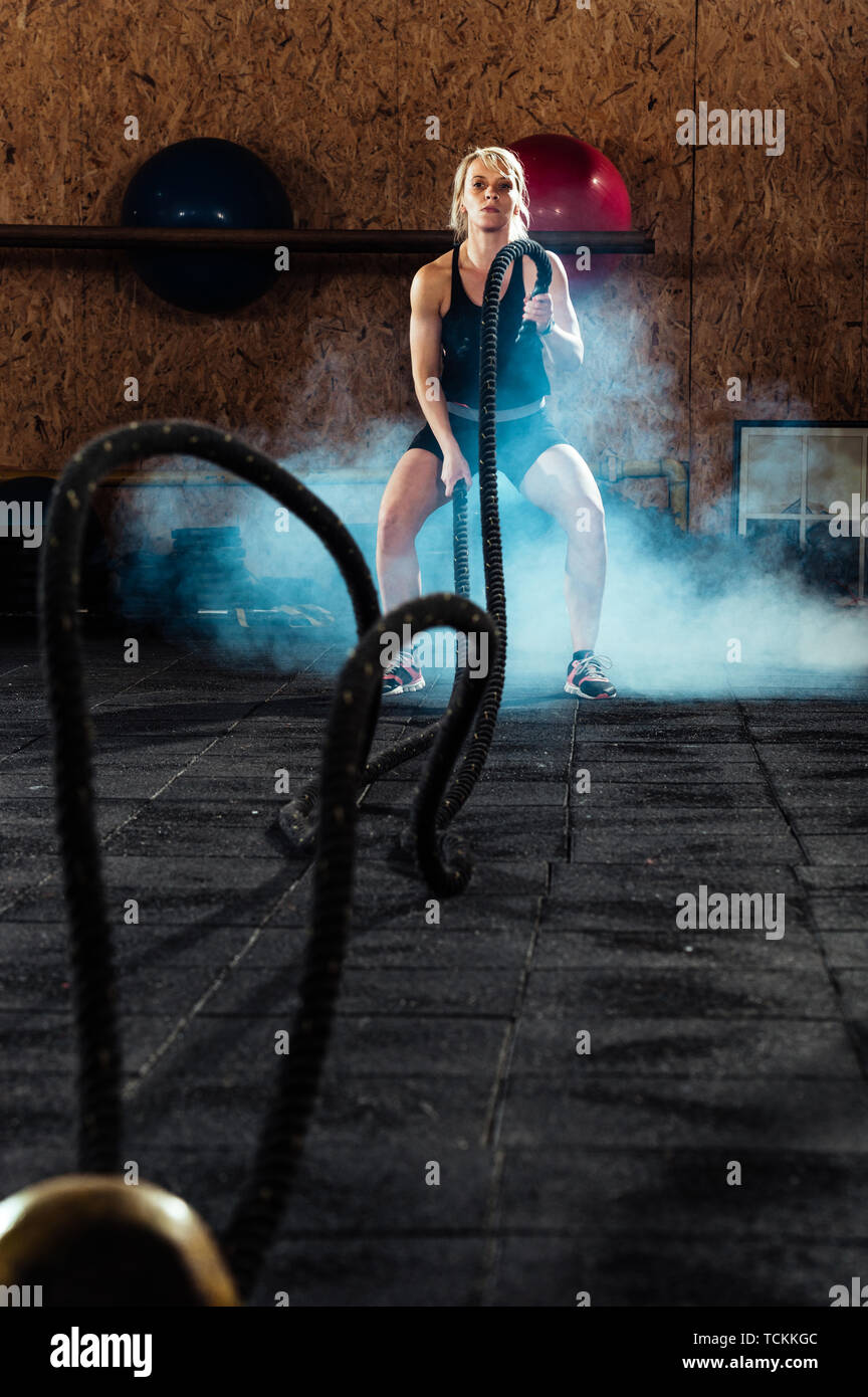 Attractive muscular woman working out with heavy ropes in crossfit ...