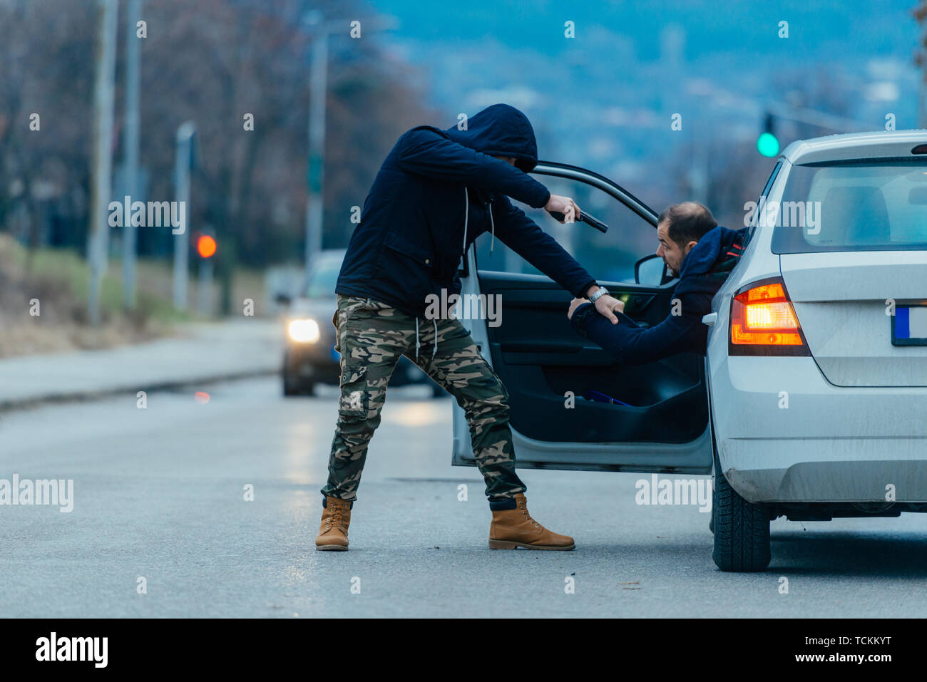 The car thief is pulling the car owner out of his car and trying to get ...