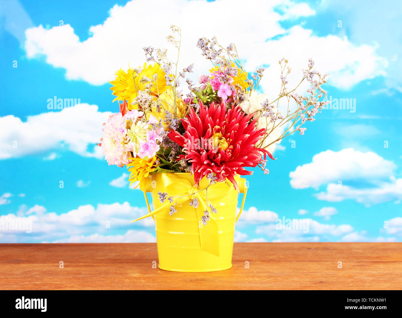 Bright yellow bucket with flowers on sky background Stock Photo - Alamy
