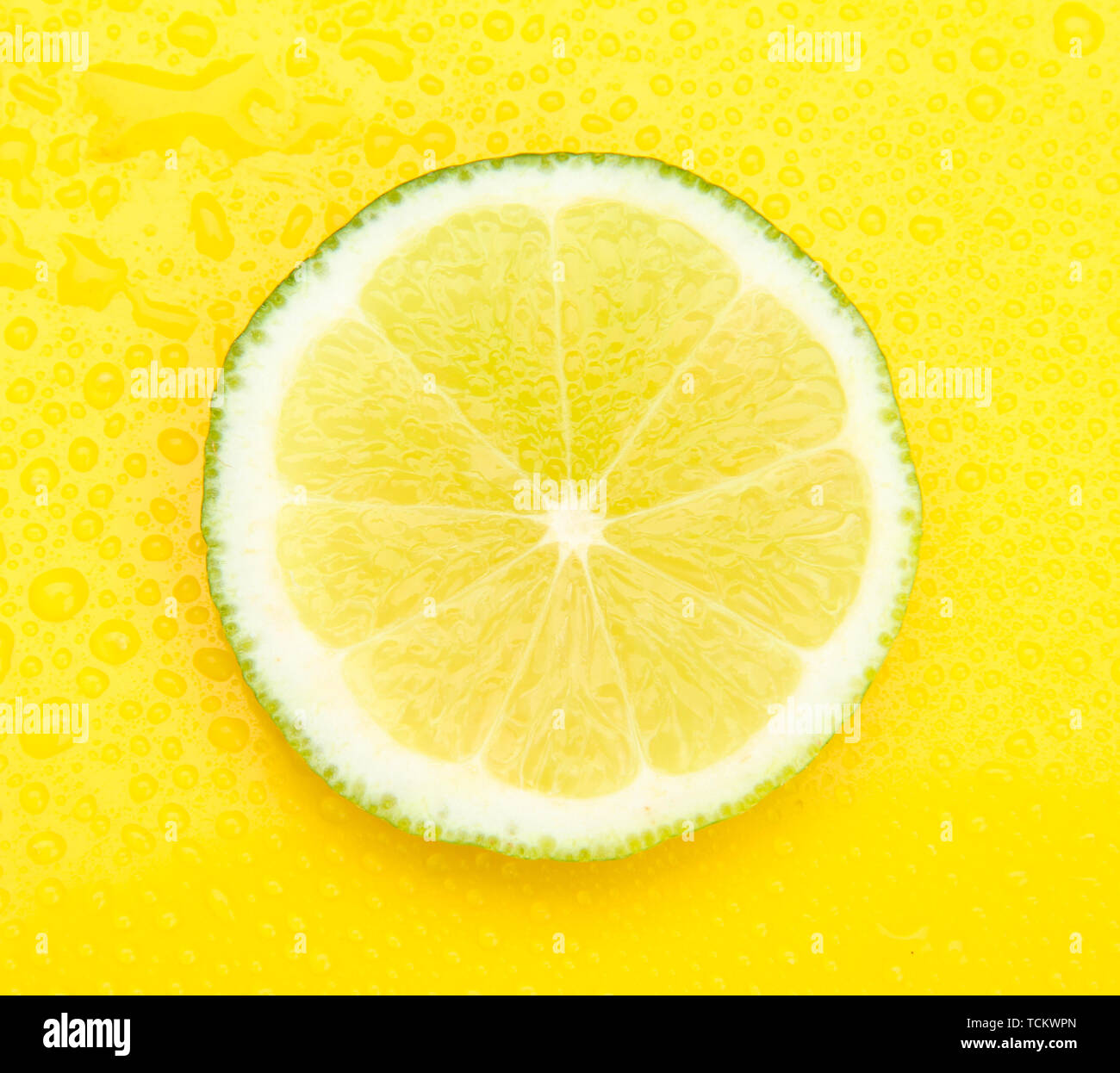 Slice of lime with drop on yellow background Stock Photo - Alamy