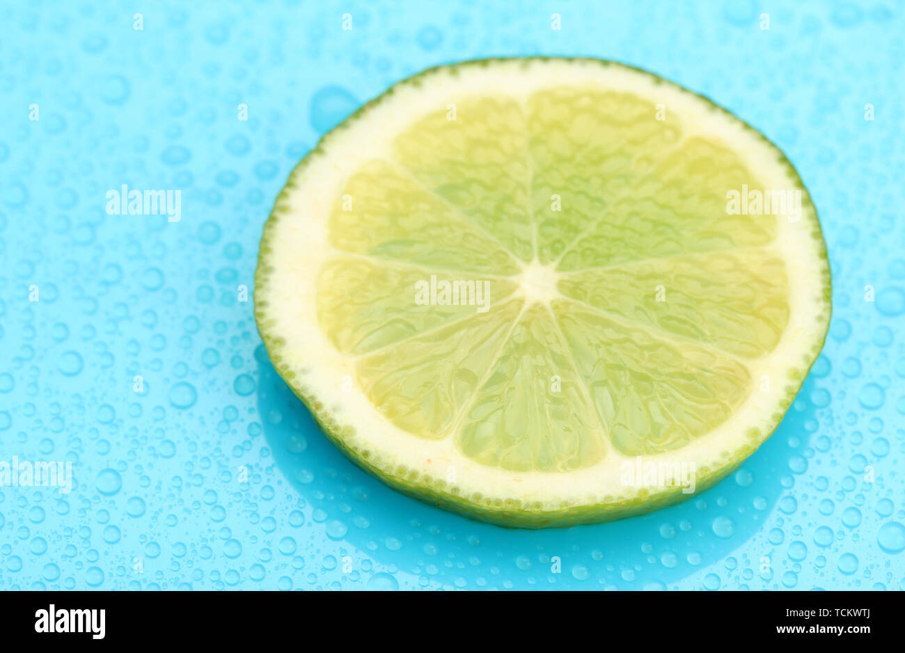 Slice of lime with drop on blue background Stock Photo - Alamy