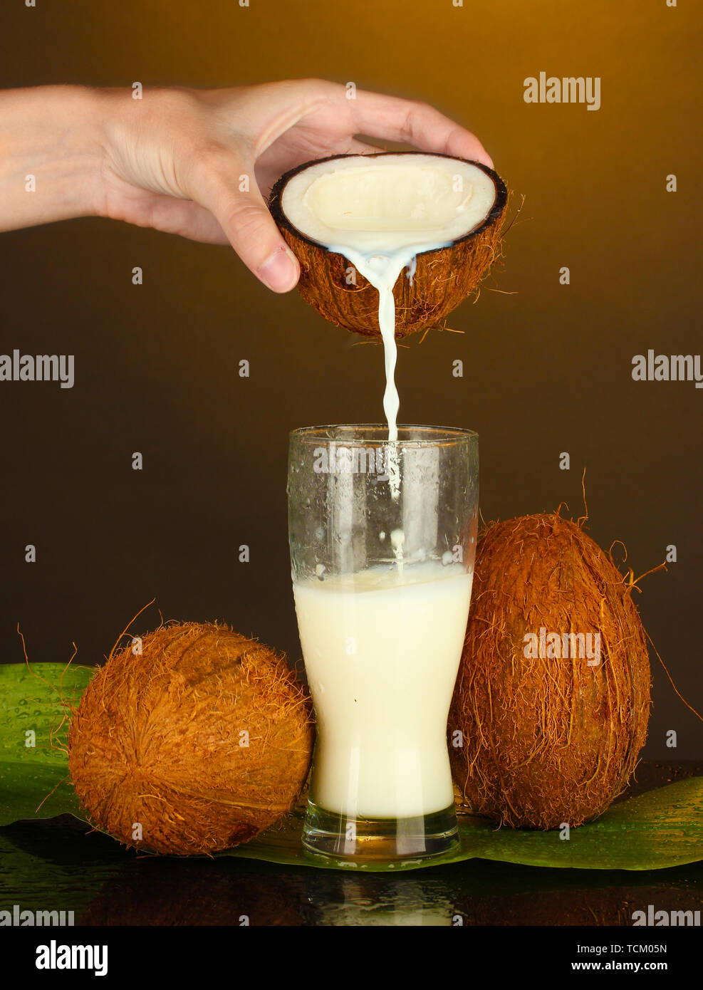 woman's hand pouring coconut milk into a glass on brown background ...
