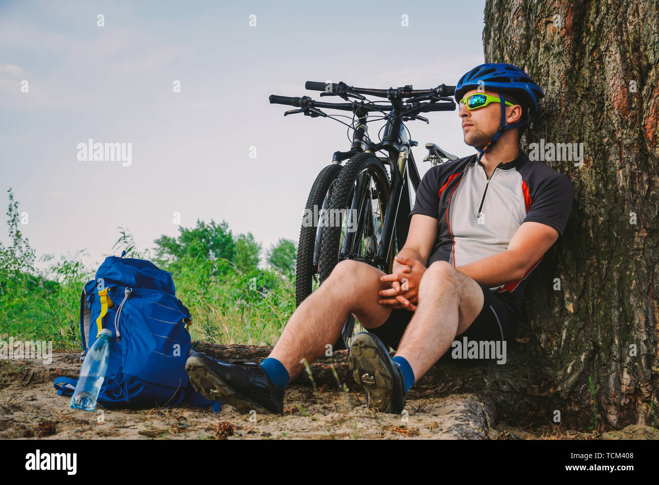 male mountain biker resting on bike ride, sitting on ground under a ...
