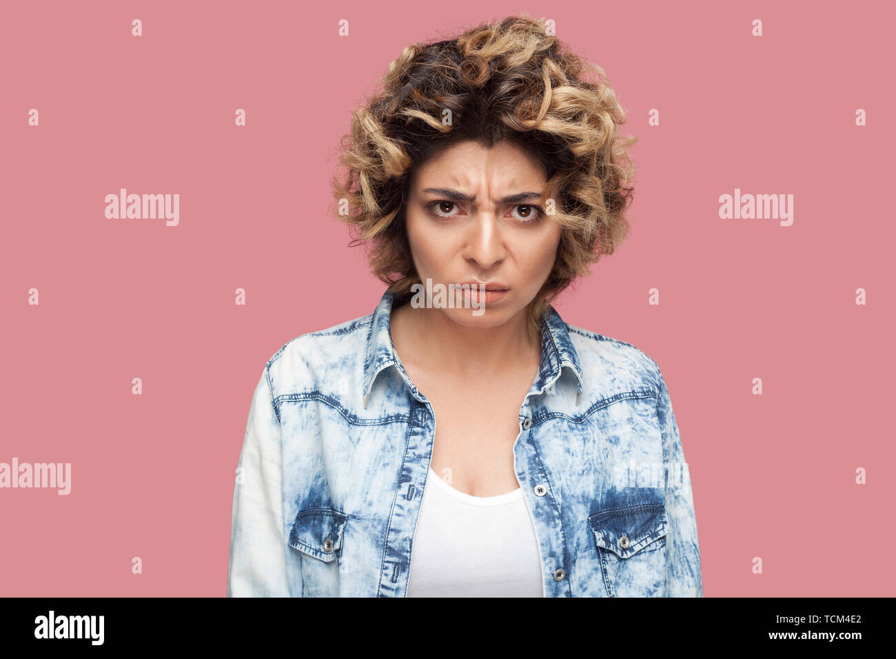Portrait of angry young woman with curly hairstyle in casual blue shirt ...