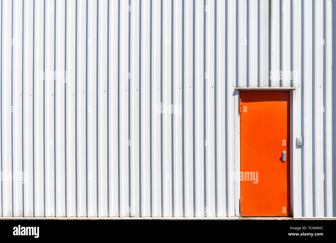 Industrial building facade with a metal orange door and a white ...