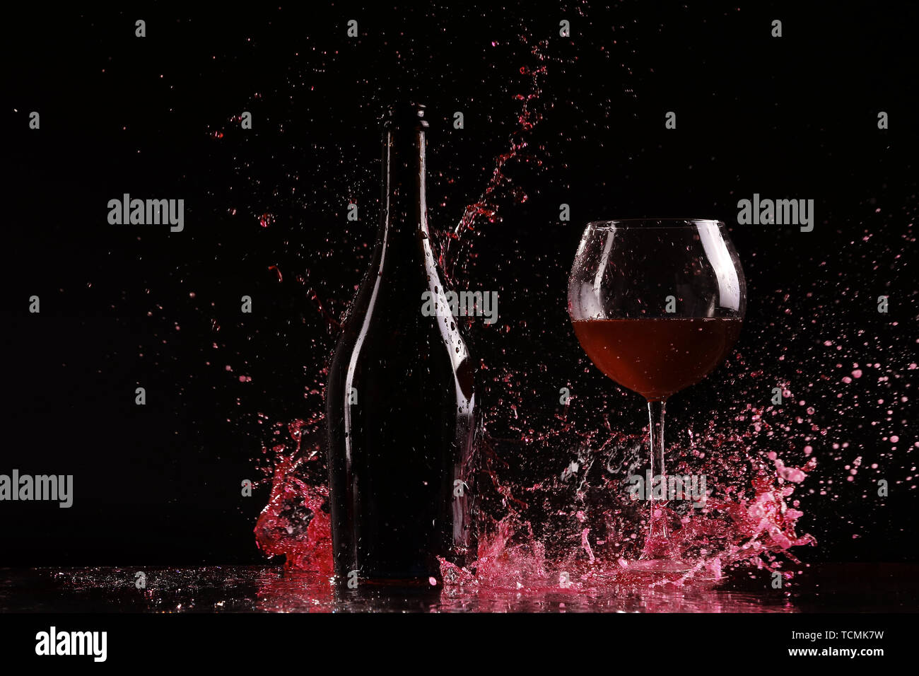 bottle with red wine, water splash, wine on table on black background ...