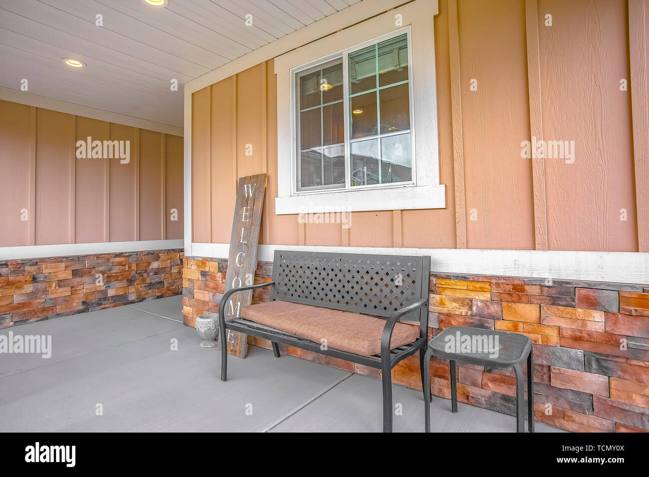 Front porch of a home with a bench and stool in front of the window ...