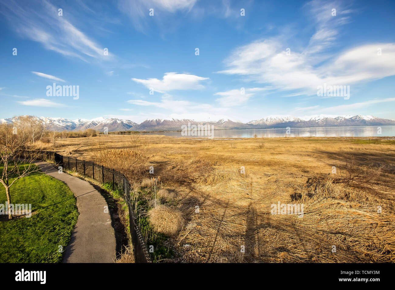 Paved pathway and fence along the shore of a lake with brown grasses ...