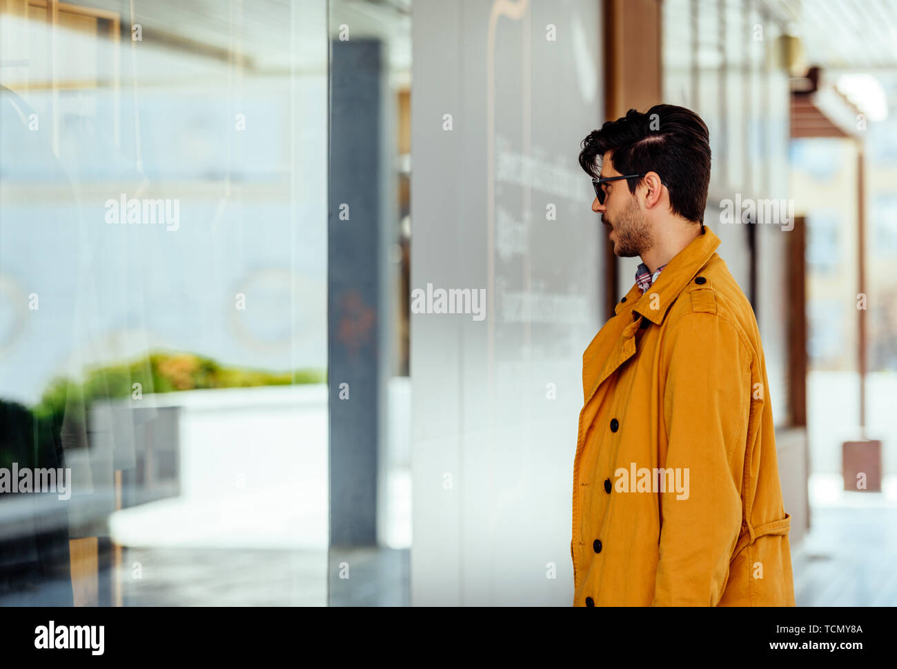 Attractive man looking in the storefront window at shopping center ...