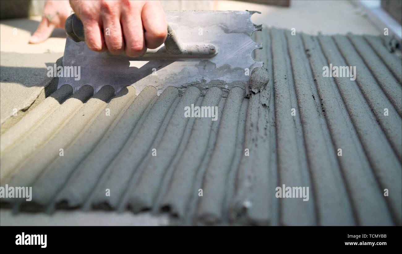 Worker with a spatula and mortar. The builder on his knees flattens the ...