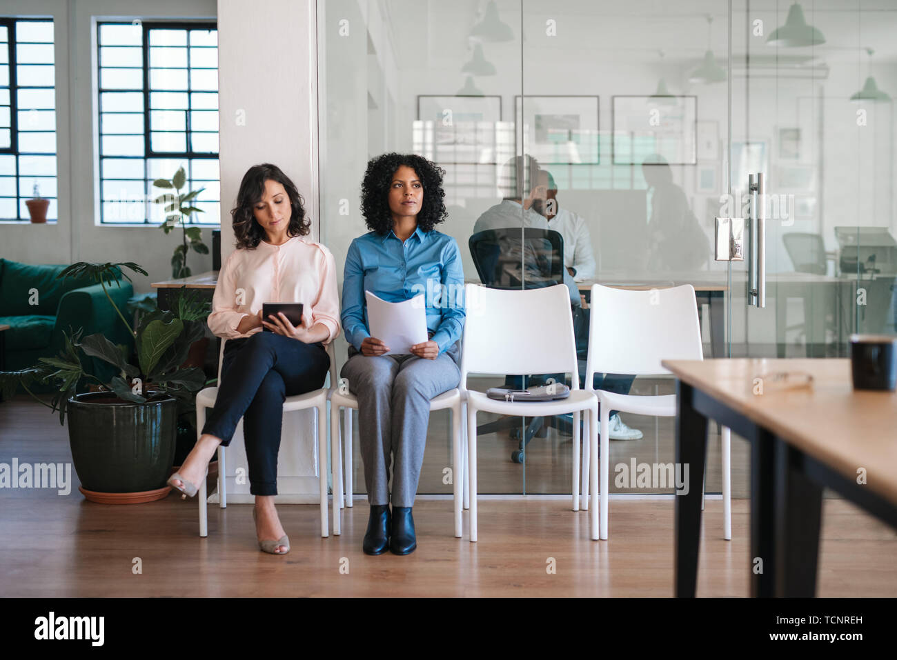 Two female job applicants sitting together outside of an office waiting ...