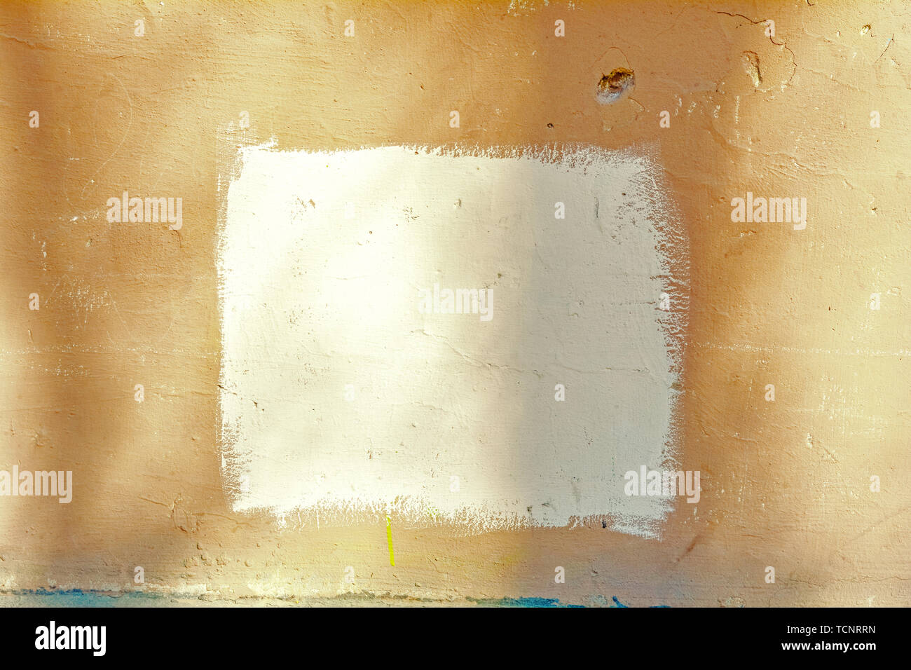 Orange rough concrete wall with a cracks and a painted white square ...