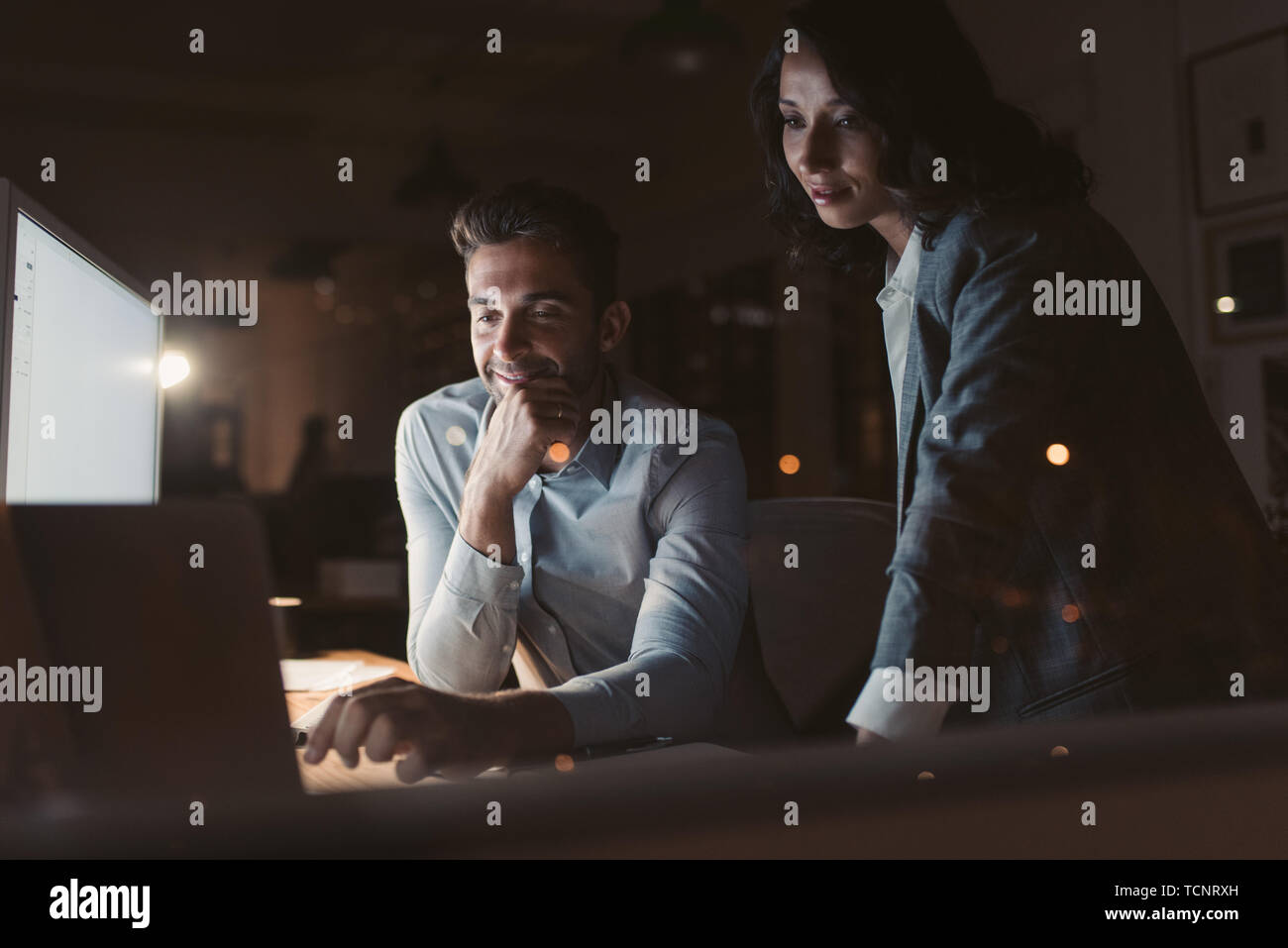 Two young colleagues smiling while working together at a desk in the ...