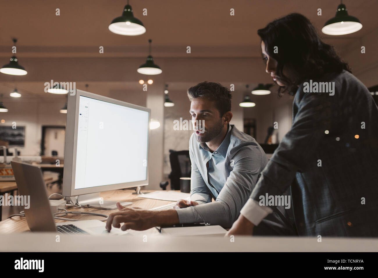 Two young office colleagues using a computer at a desk while working ...