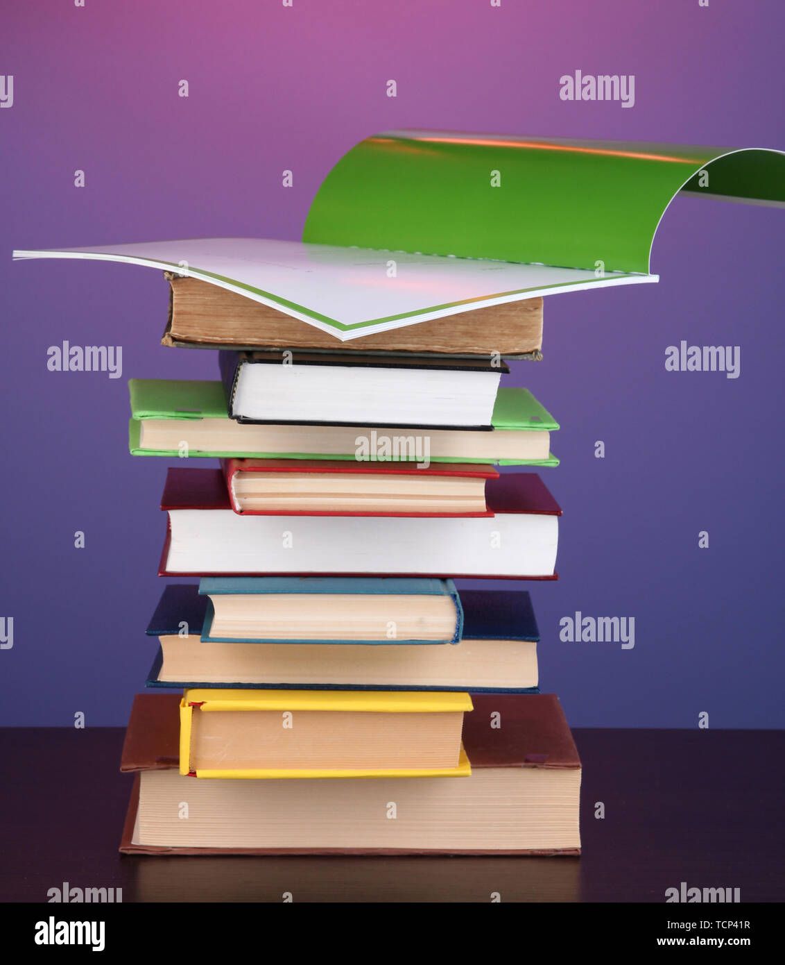 Stack of interesting books and magazines on wooden table on purple ...