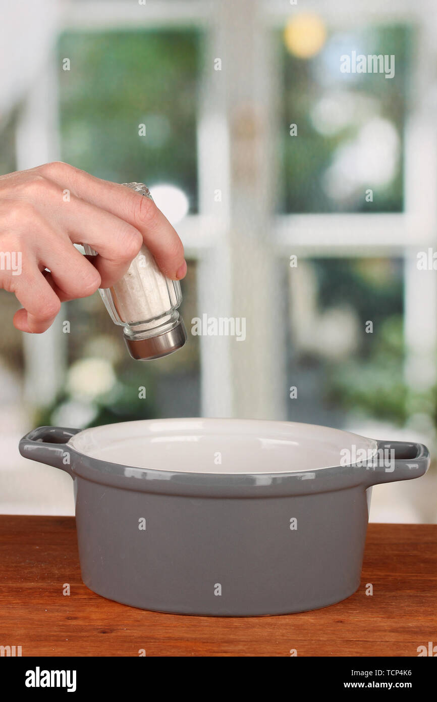 Hand adding salt using salt shaker on bright background Stock Photo - Alamy