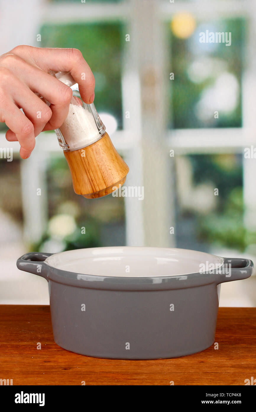 Hand adding salt using salt shaker on bright background Stock Photo - Alamy