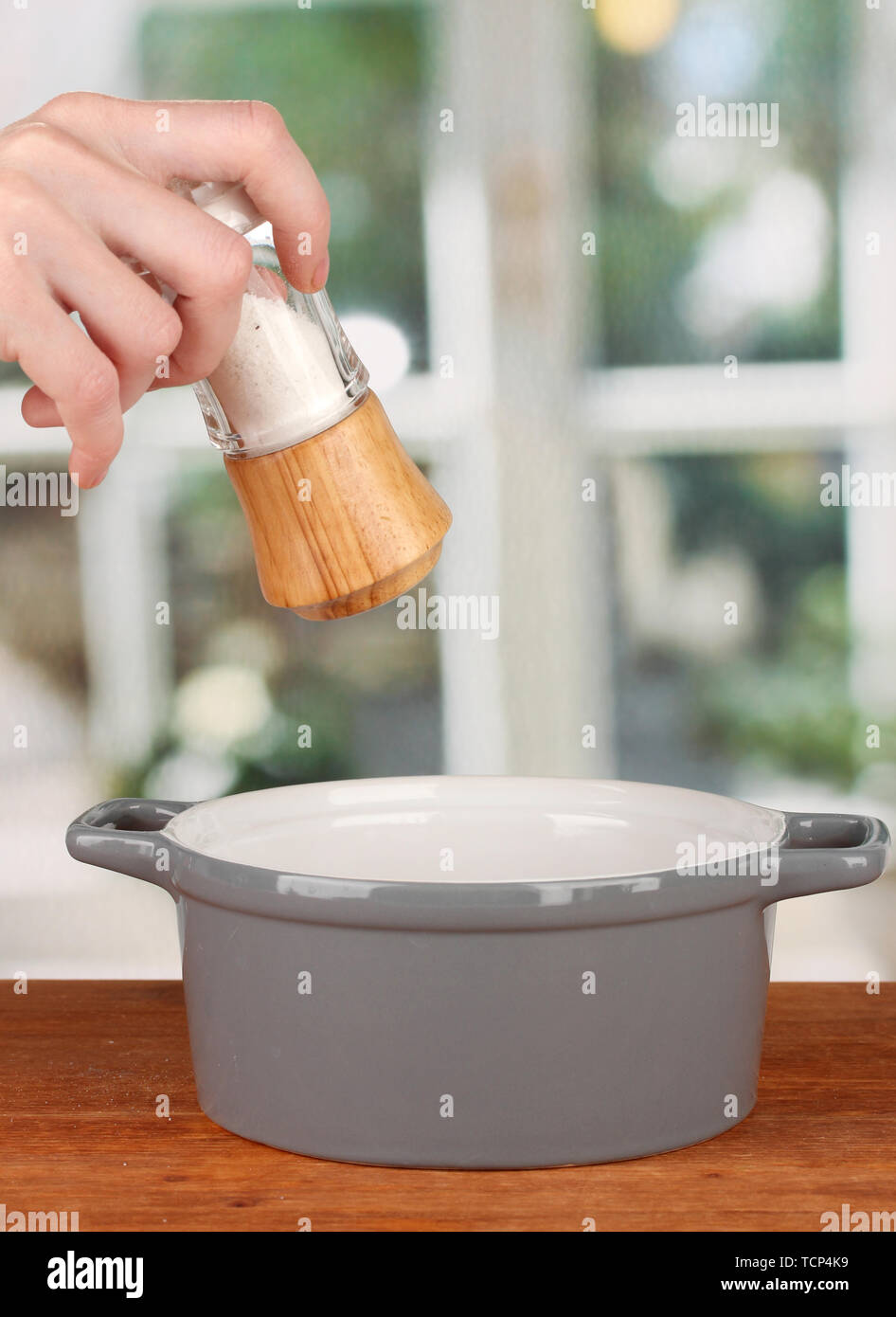 Hand adding salt using salt shaker on bright background Stock Photo - Alamy