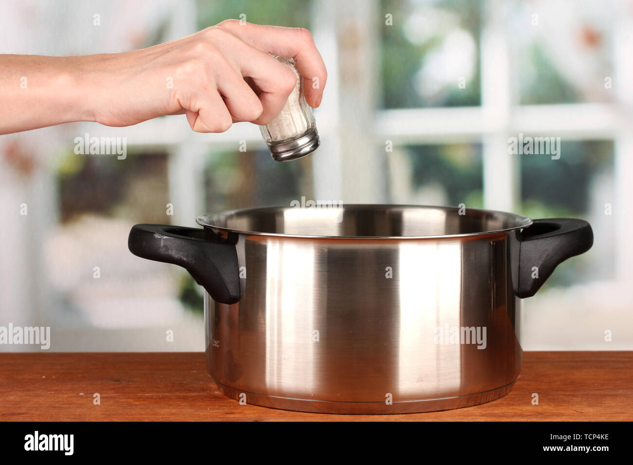 Hand adding salt using salt shaker on bright background Stock Photo - Alamy