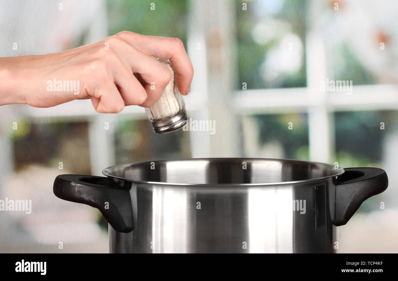 Hand adding salt using salt shaker on bright background Stock Photo - Alamy