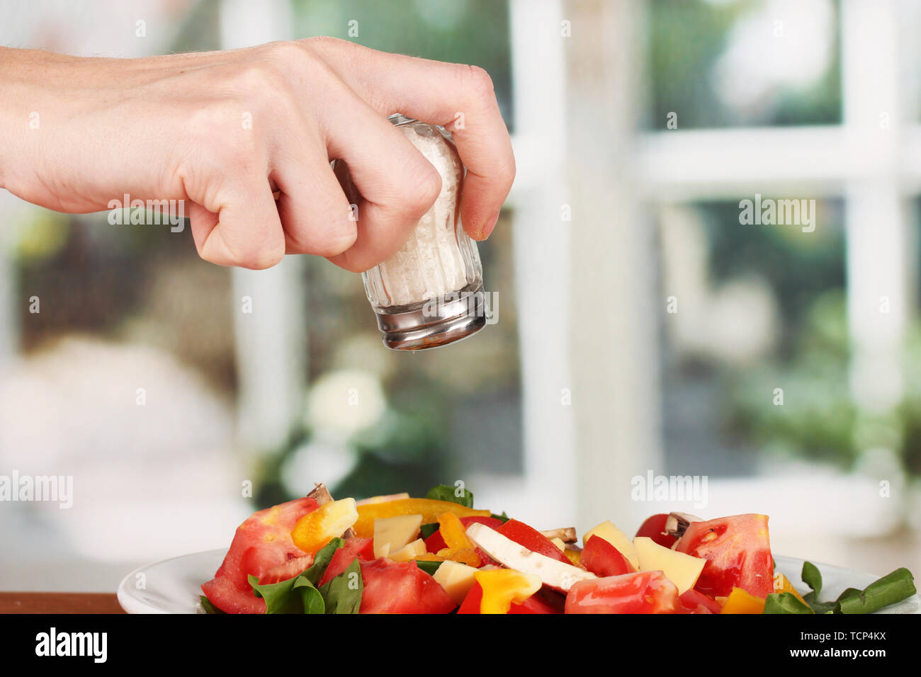Hand adding salt using salt shaker on bright background Stock Photo - Alamy