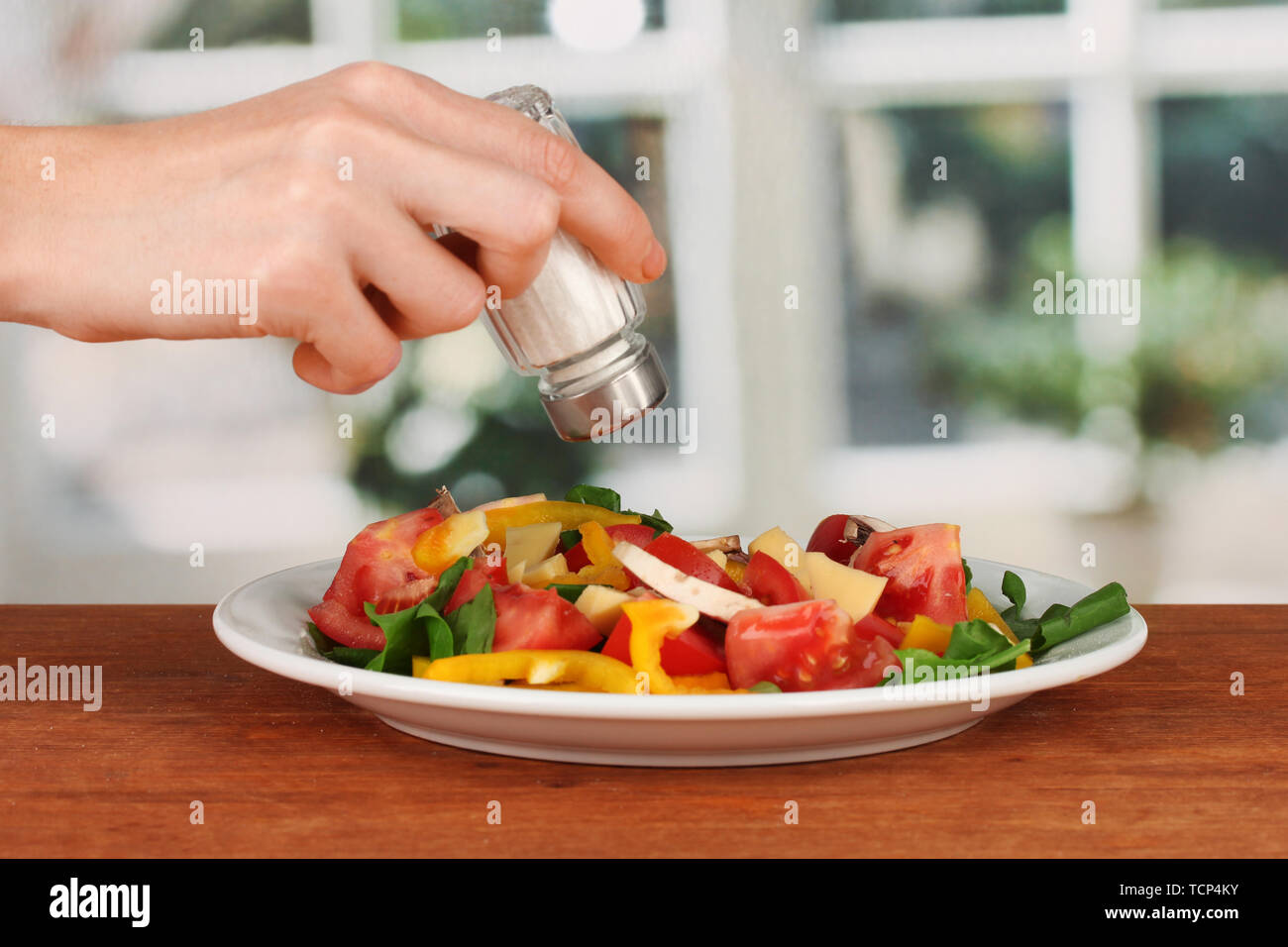 Hand adding salt using salt shaker on bright background Stock Photo - Alamy