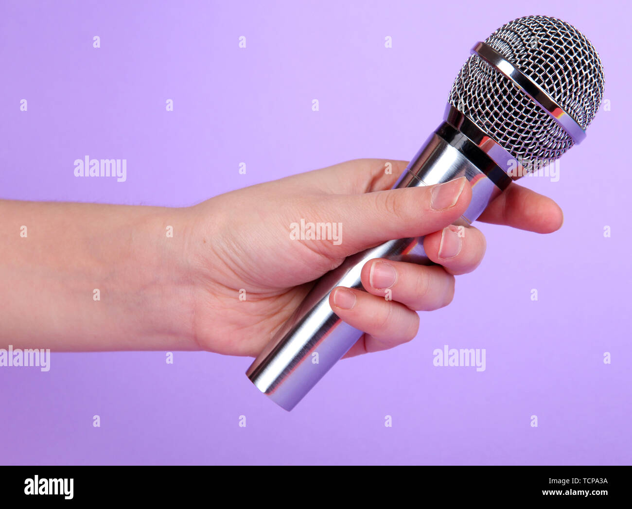 Silver microphone in hand on purple background Stock Photo - Alamy