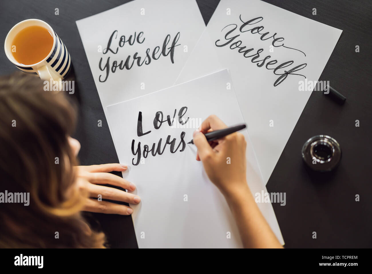 Love yourself. Calligrapher Young Woman writes phrase on white paper ...