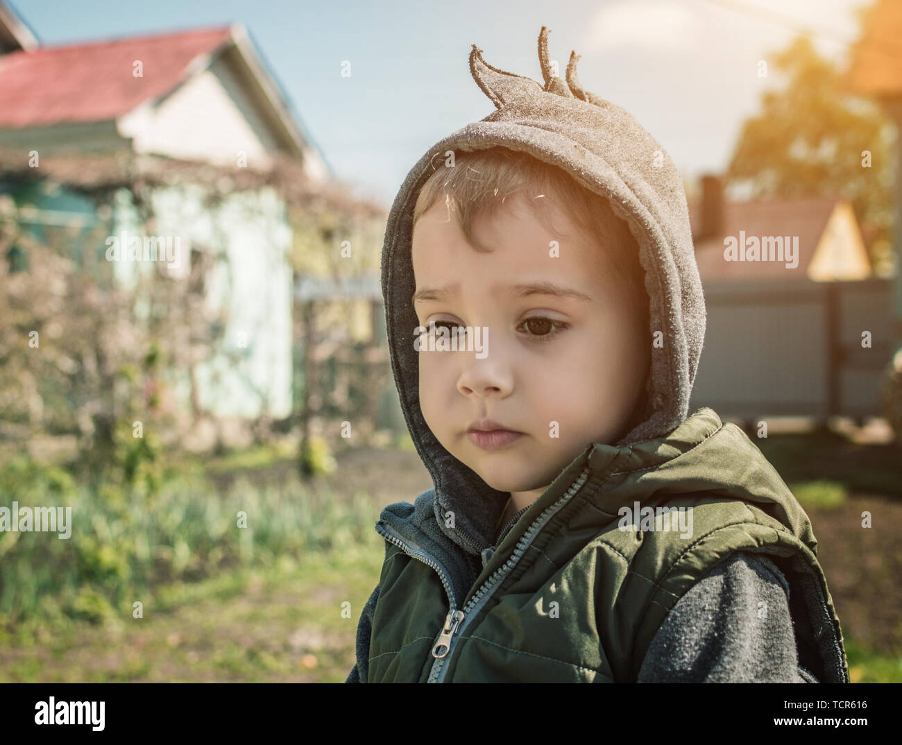 child with a sad face, portrait against the backdrop of a village house ...