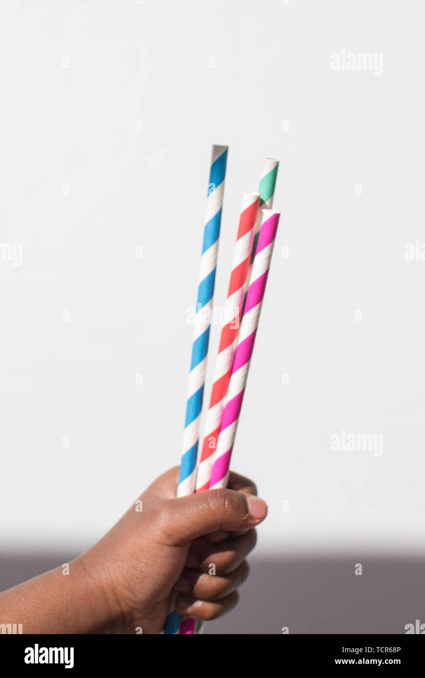 A young asian girl aged 5 holding paper straw in her hands over plain ...