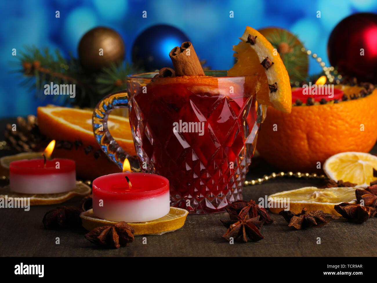 Fragrant mulled wine in glass with spices and oranges around on wooden ...