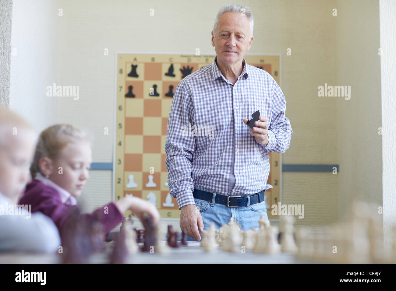Aged male teacher showing chess figure and explaining chess moves for ...