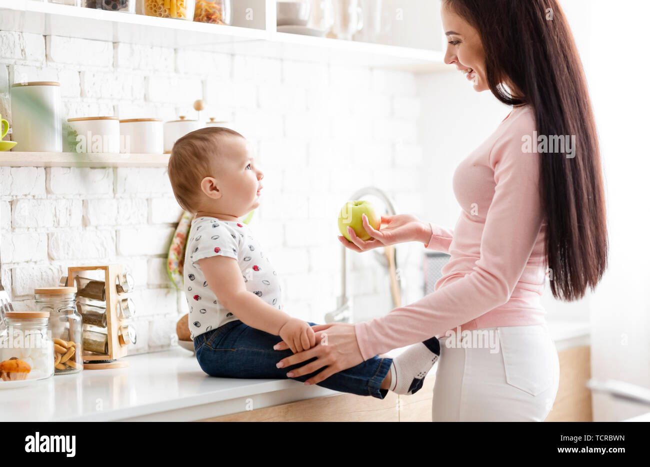 Lovely mother offering fresh green apple to her cute baby Stock Photo ...