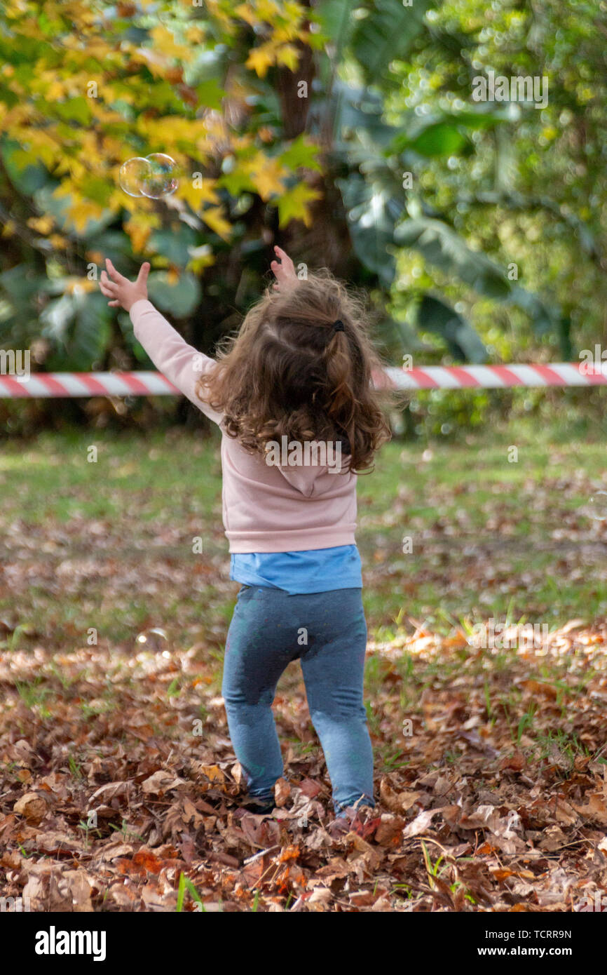 A close up view of a little girl running though a park catching bubbles ...