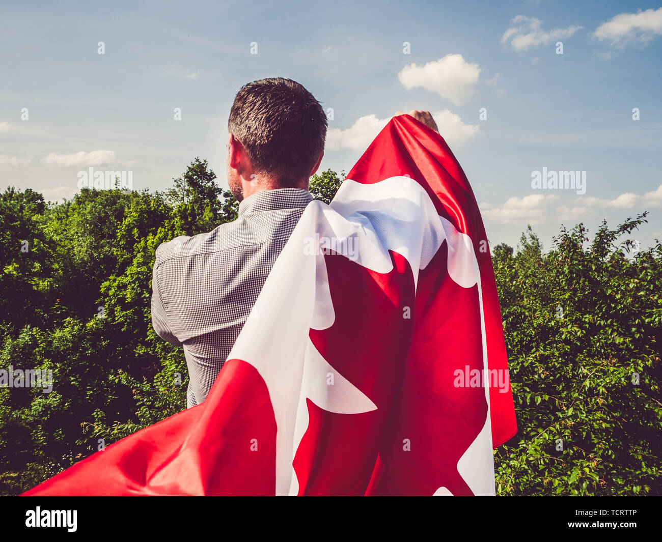 Handsome man waving a Canadian Flag against a background of trees and ...