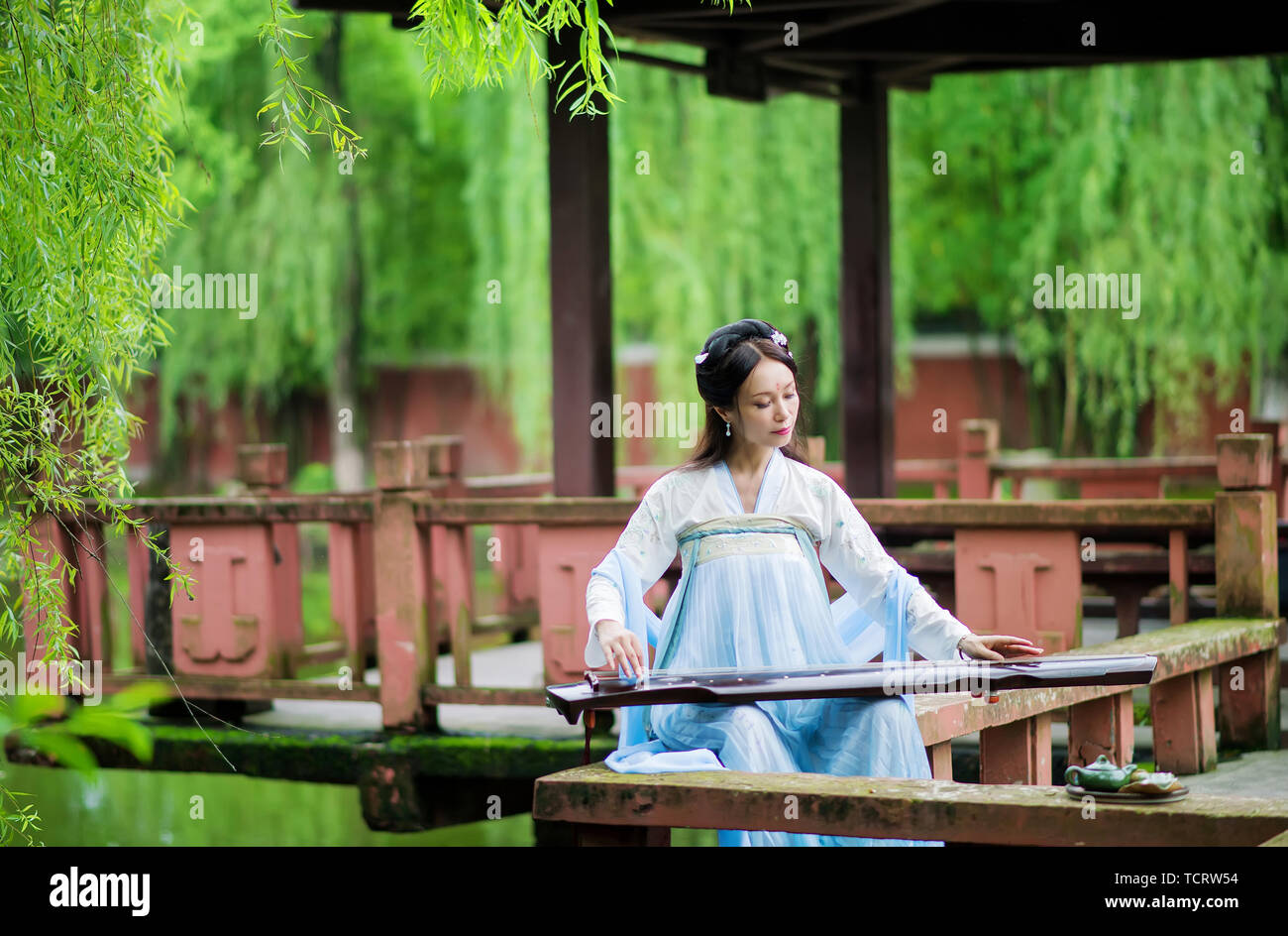 A woman in a Chinese dress is playing the Guqin Stock Photo - Alamy