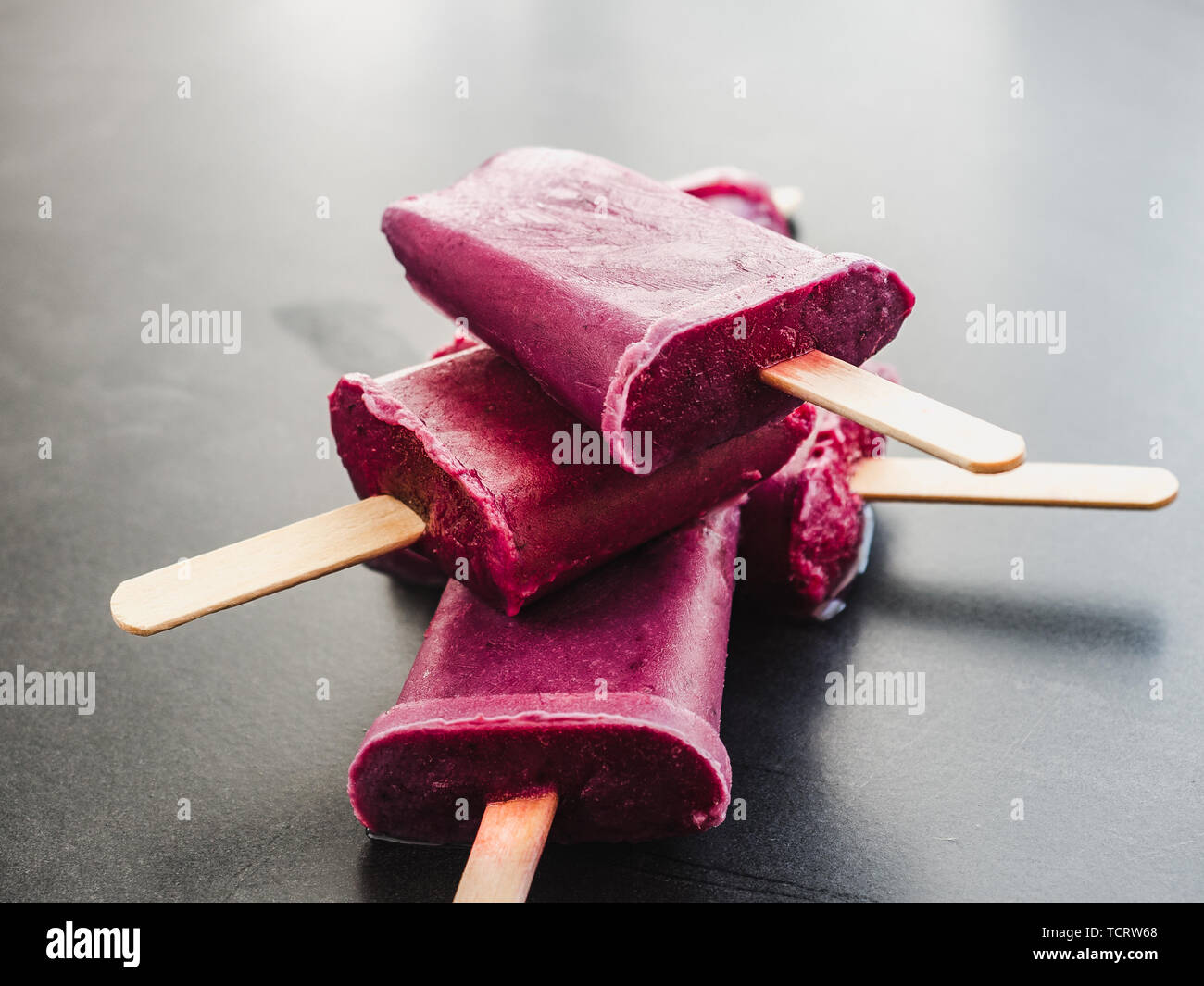 Bright, fruity red ice cream with wooden sticks on a black table. Close ...