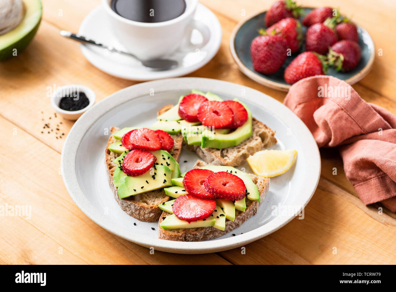 Rye toast with avocado and strawberry for breakfast. Cup of coffee on ...