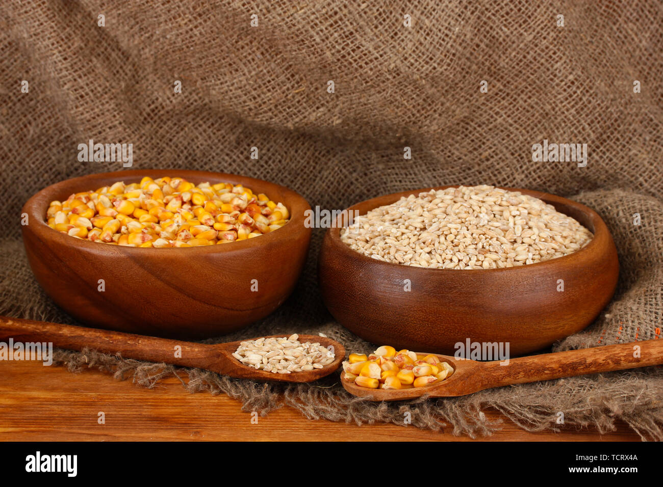 Raw corn and wheat in wooden bowls on table on sackcloth background ...