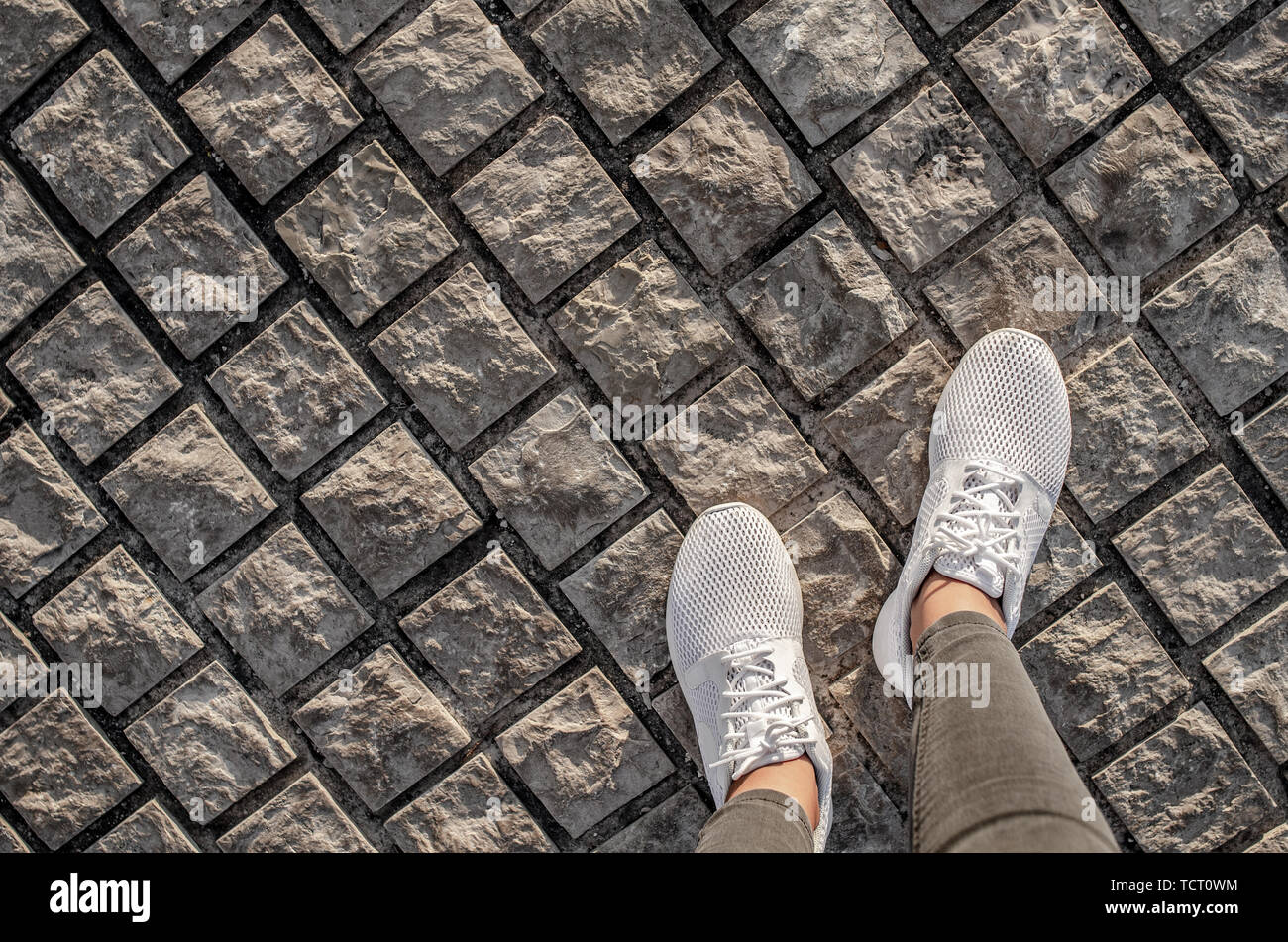 Women's legs in white sneakers on the stone pavement Stock Photo - Alamy